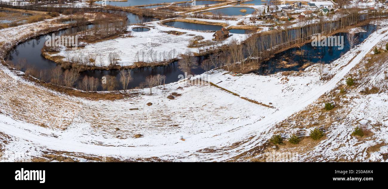 A winter scene features frozen ponds surrounded by sparse trees and ...