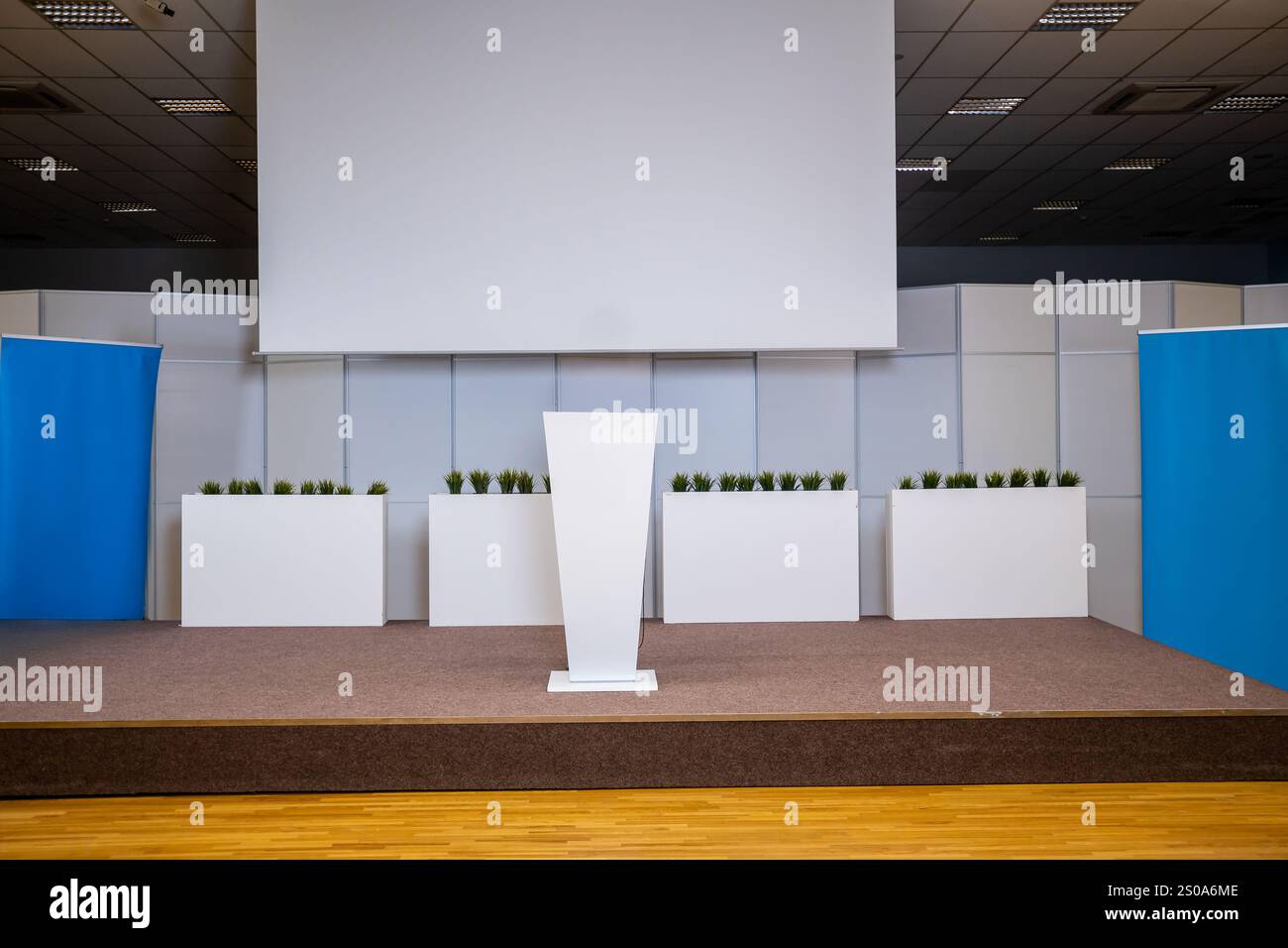 An indoor conference setting features a podium on stage, a large white ...