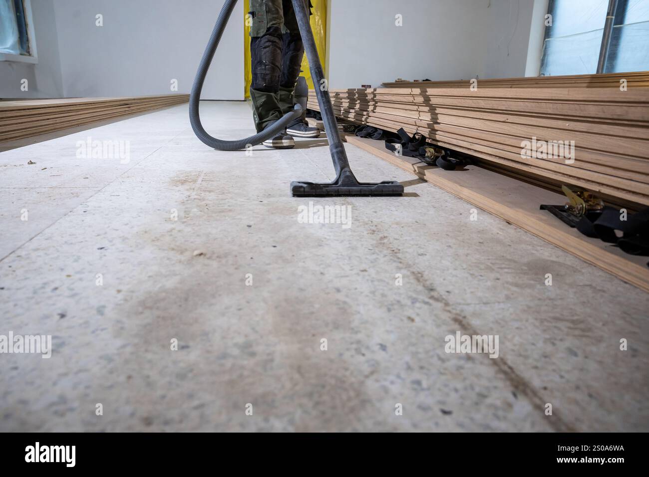 A construction worker uses a vacuum cleaner on a concrete subfloor ...