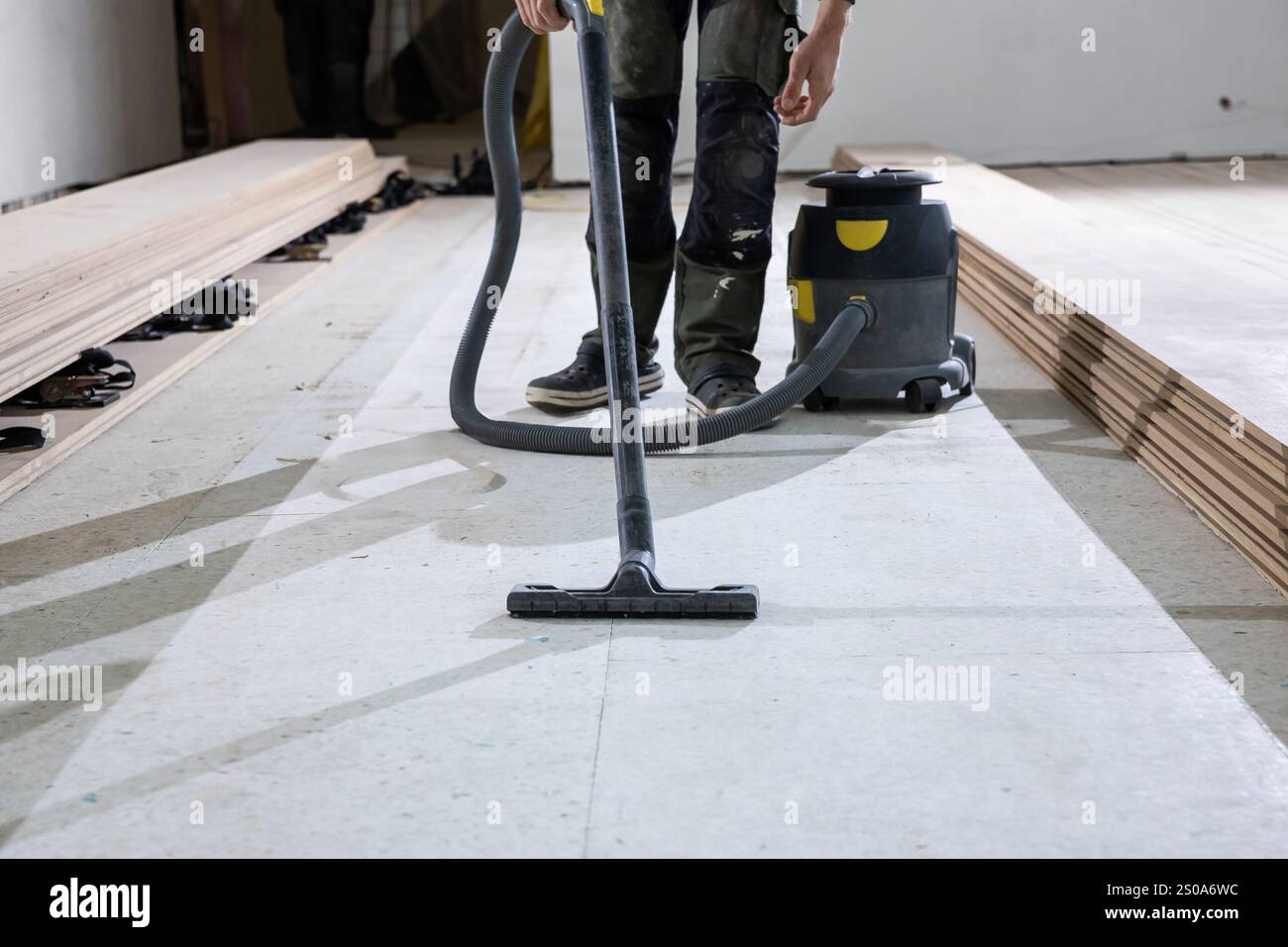 A worker uses a vacuum cleaner to clean a floor before installing ...