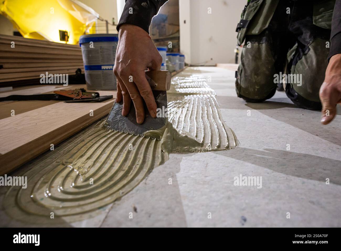 A person uses a notched trowel to apply adhesive in parallel lines on a ...