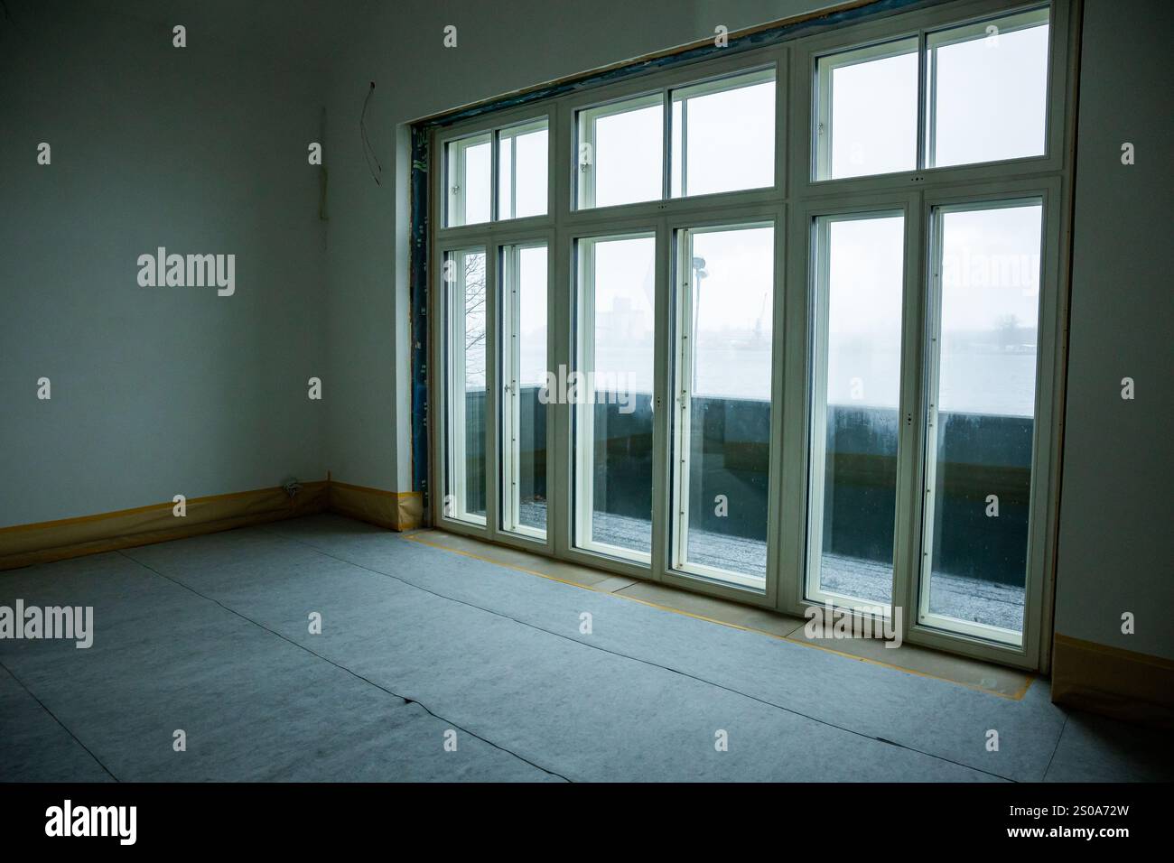 An empty room features large windows opening to a balcony, revealing a ...