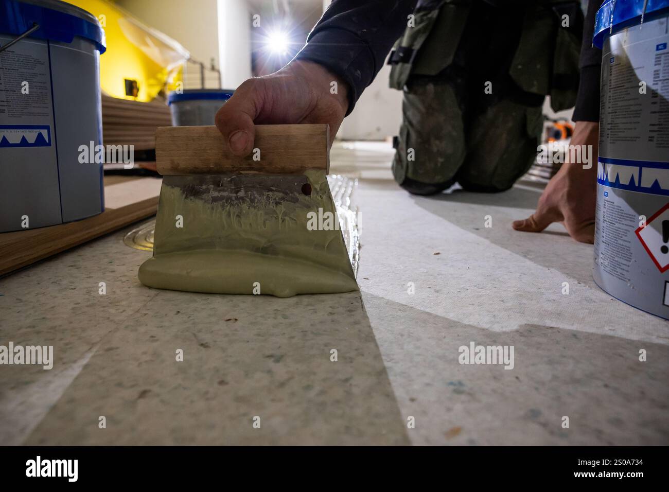 A detailed view of a person using a trowel to apply adhesive on a floor ...