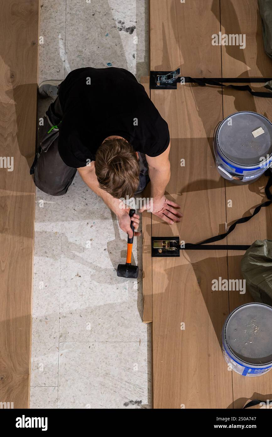 A person uses a mallet to install light wood floorboards. Clamps and ...