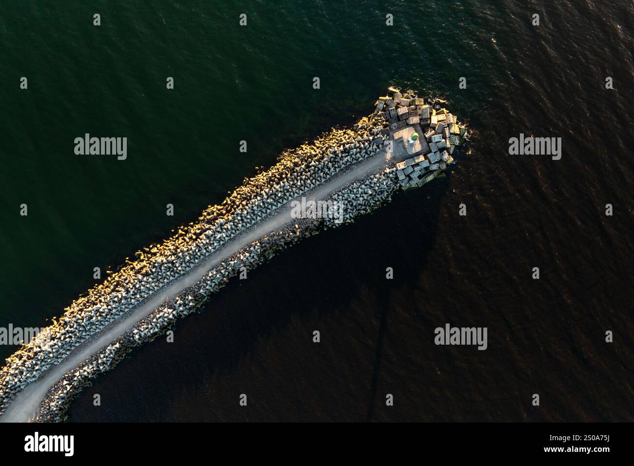 An aerial perspective of a long jetty with large rocks and concrete ...