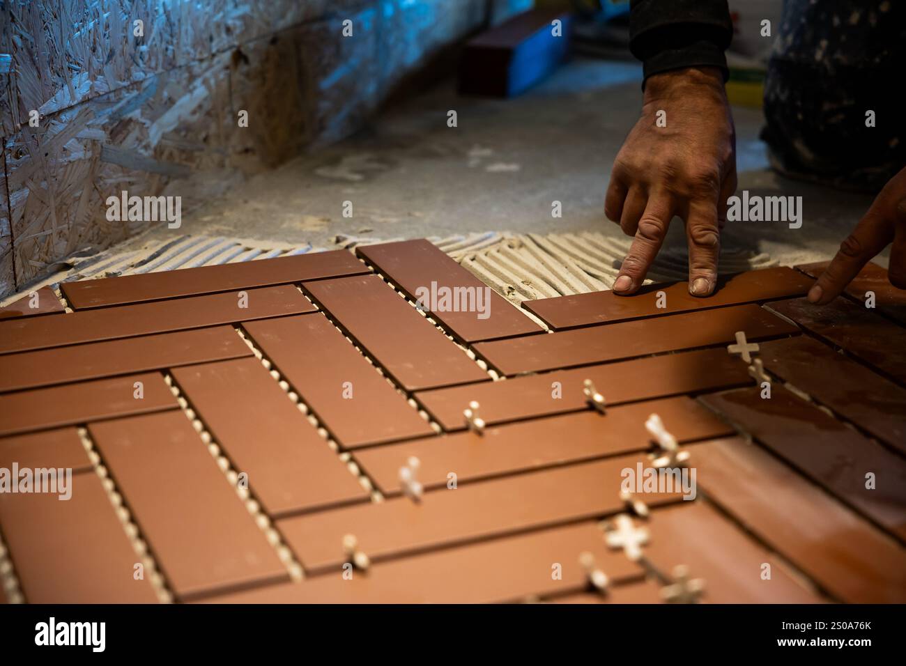 Hands position brown rectangular tiles in a herringbone pattern on a ...