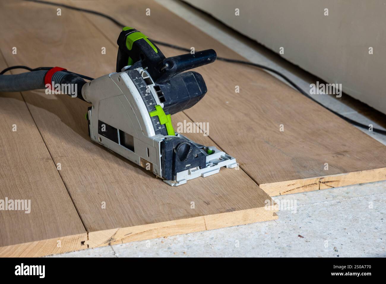 A circular saw with a dust extraction hose rests on wooden floorboards ...