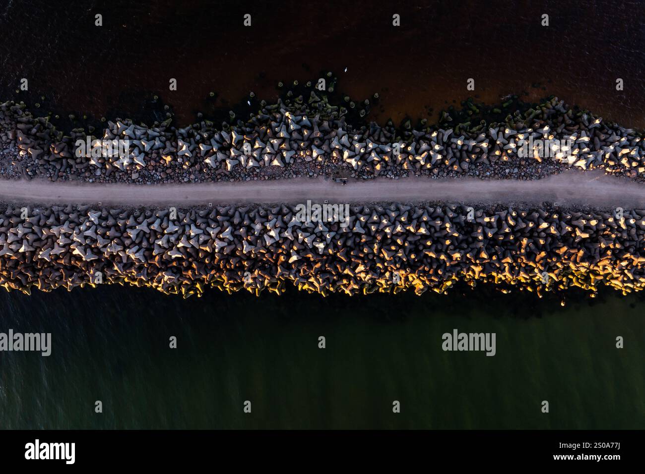 An aerial perspective of a long, narrow jetty composed of large ...