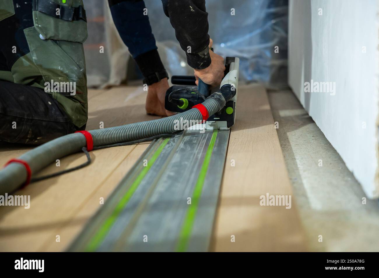 An individual in work attire uses a track saw to cut wood flooring. The ...