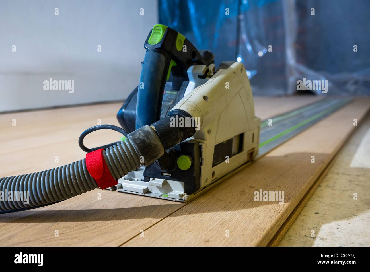 A track saw with a green and black design is set on a wooden floor ...