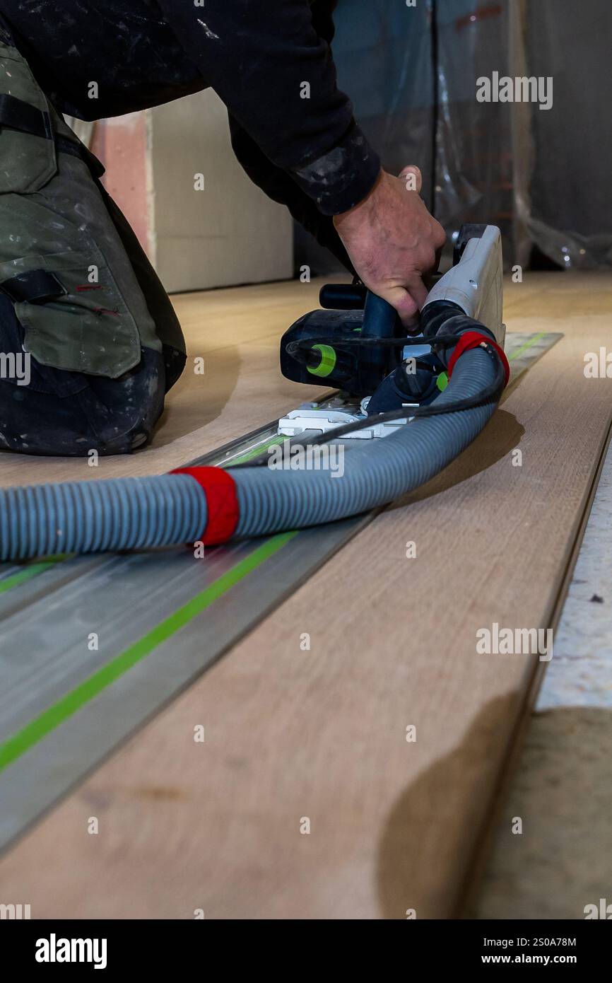 A person kneels on the floor, operating a track saw connected to a ...
