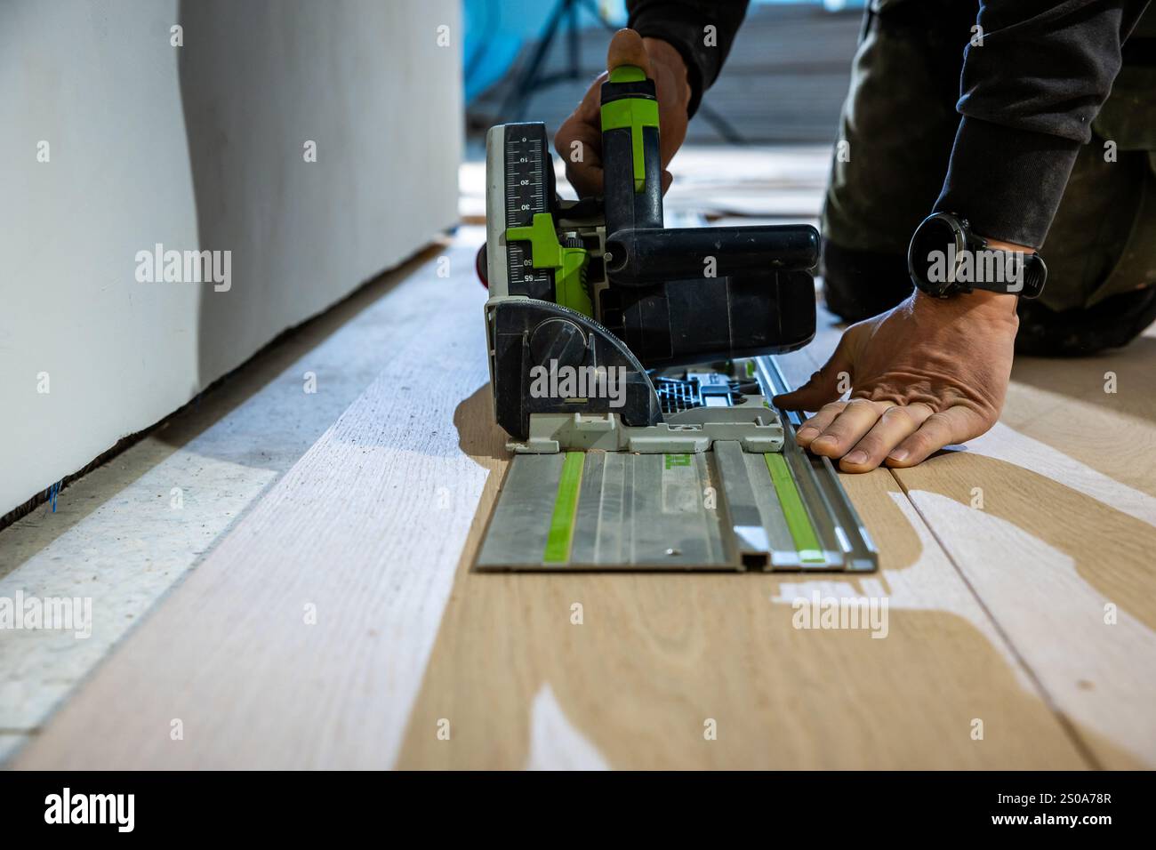 A person uses a track saw on a wooden plank, focusing on precision. The ...