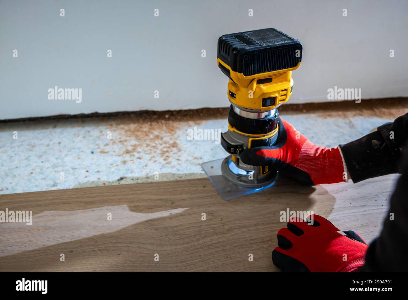 A person in red gloves operates a yellow and black router on wood, with ...
