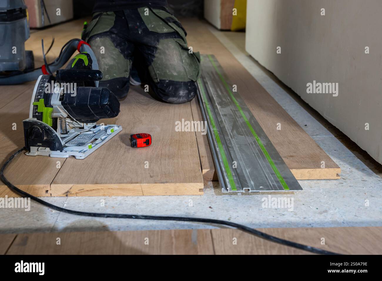 An individual kneels indoors, operating a circular saw with a metal ...