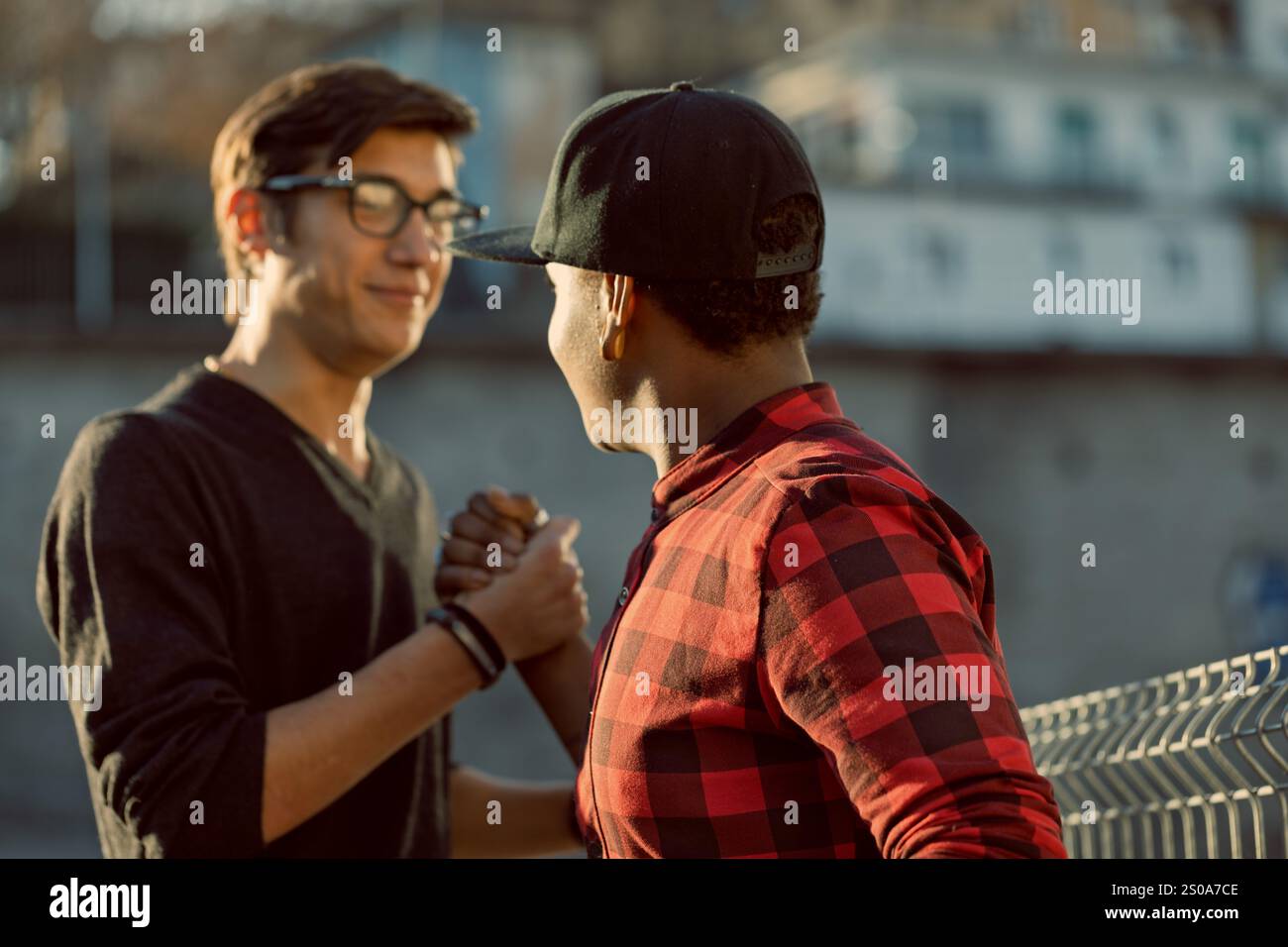 Two young men shaking hands in an urban setting, radiating friendship ...