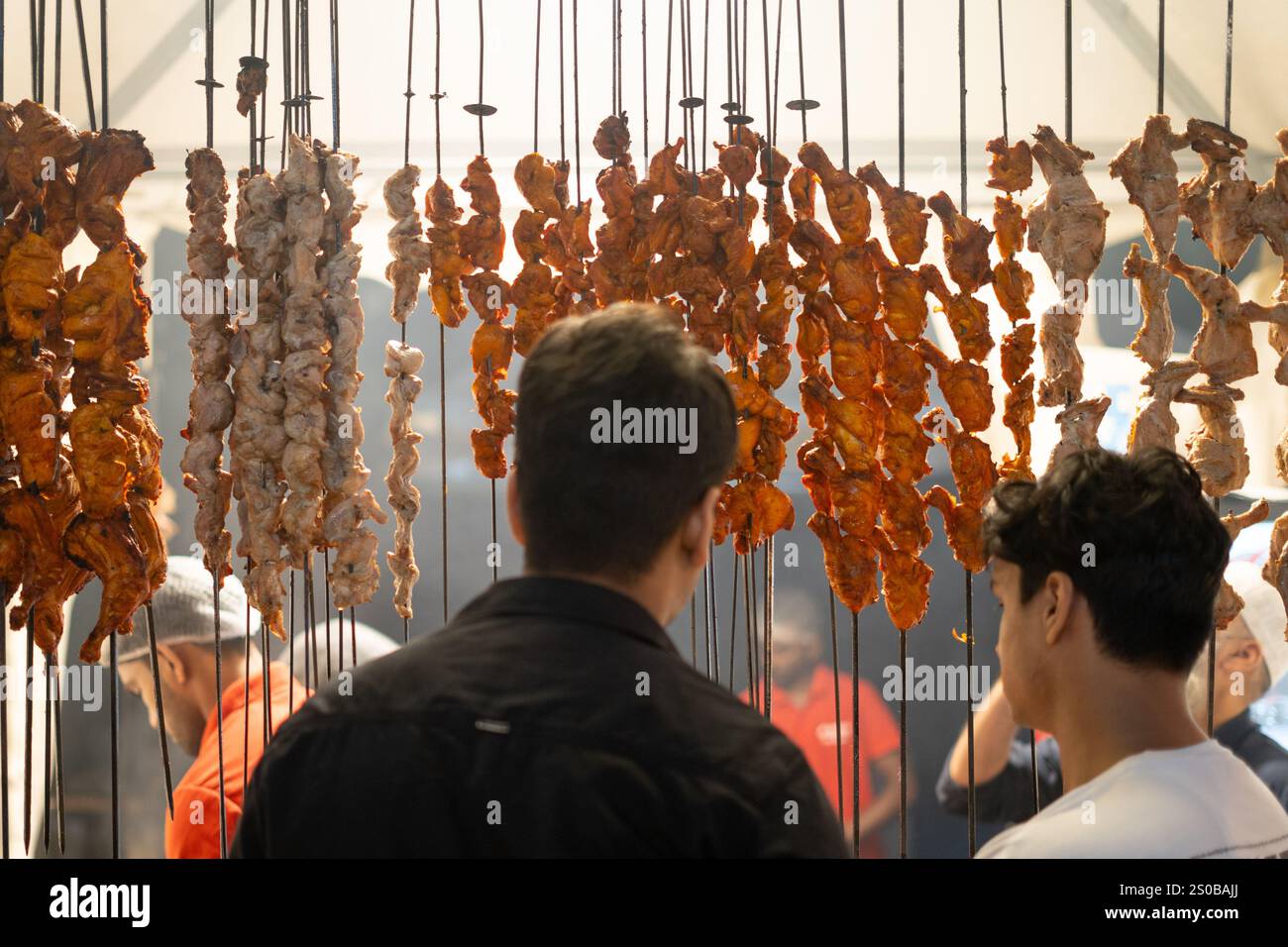 Young men standing in front of kebab meat shop with chicken hanging on ...