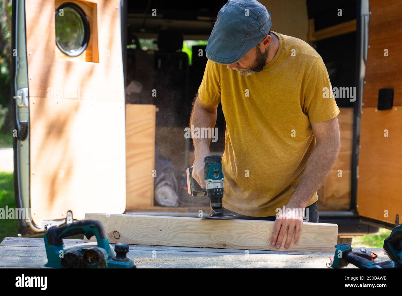 Carpenter uses cordless drill on a piece of wood near an open van ...