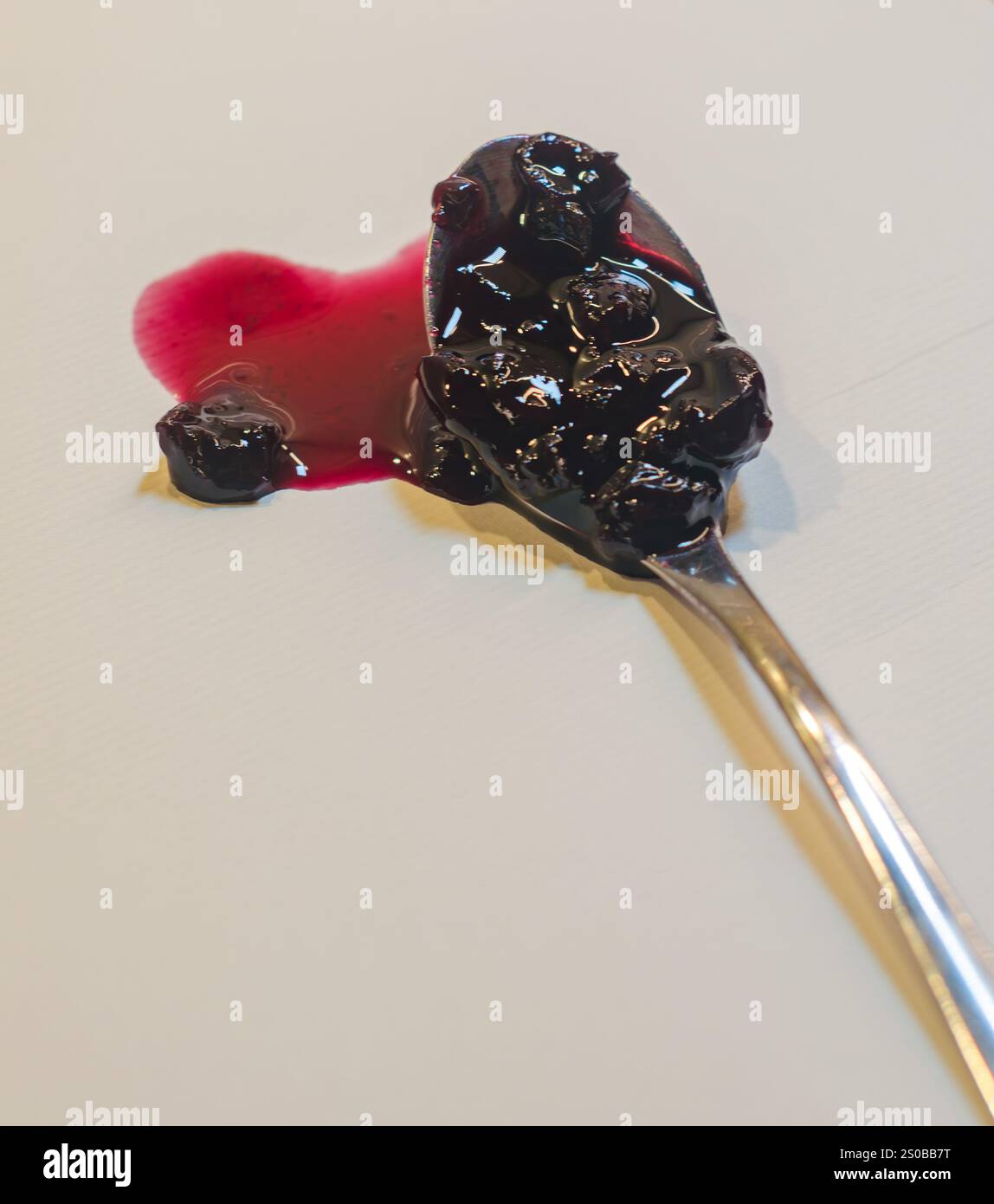 Spoon with a heart-shaped spill of dark red jam, with berries on a ...