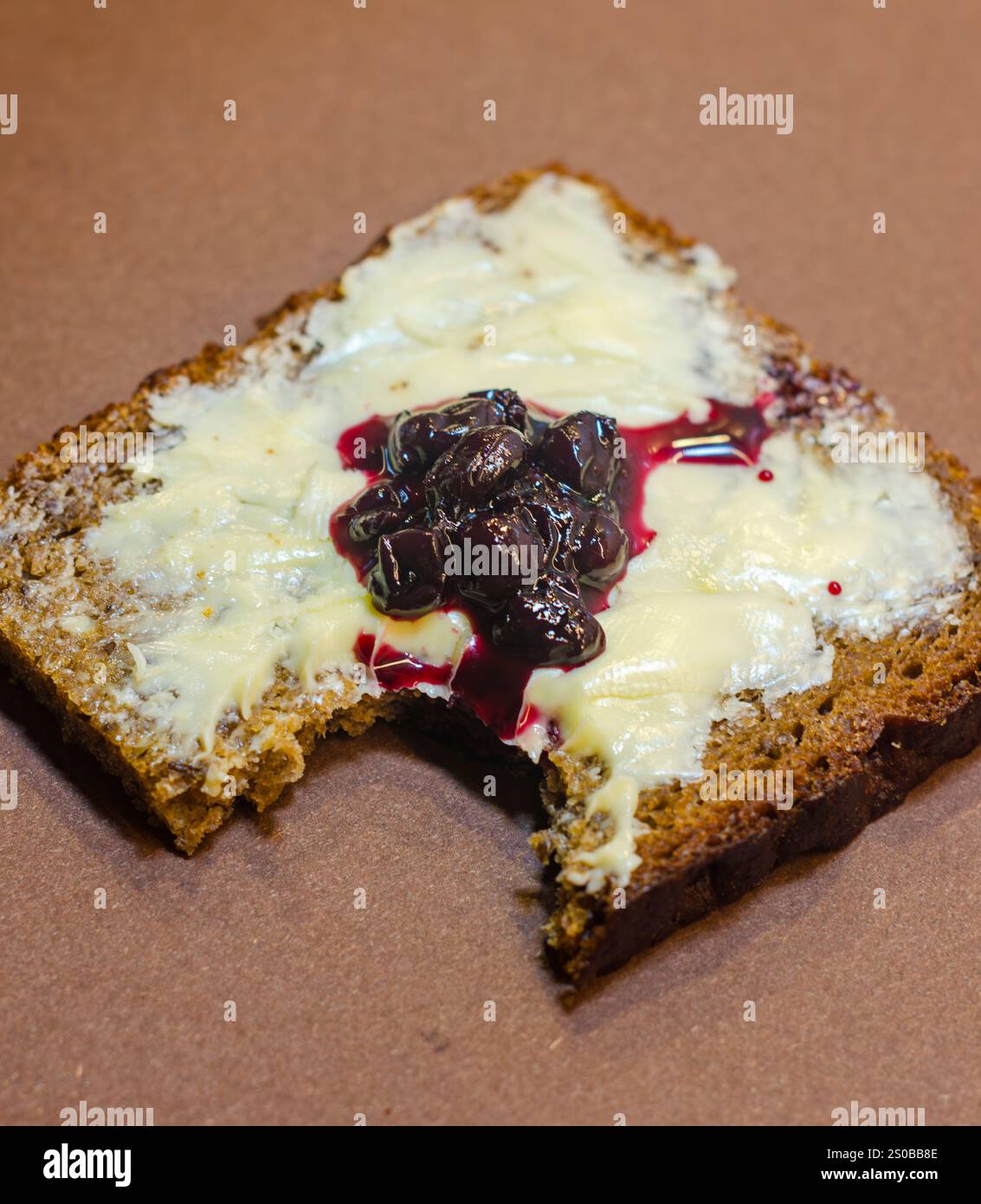 A slice of toast with butter and blueberry jam, with a bite taken out ...