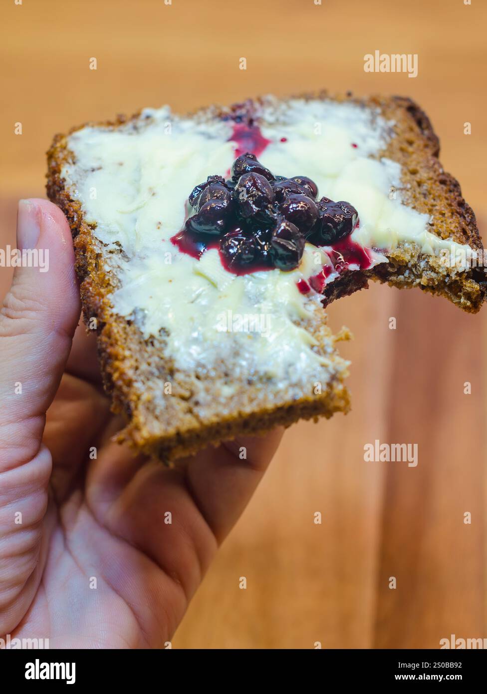 A hand holding a bite of toast with butter and wild berry jam. High ...