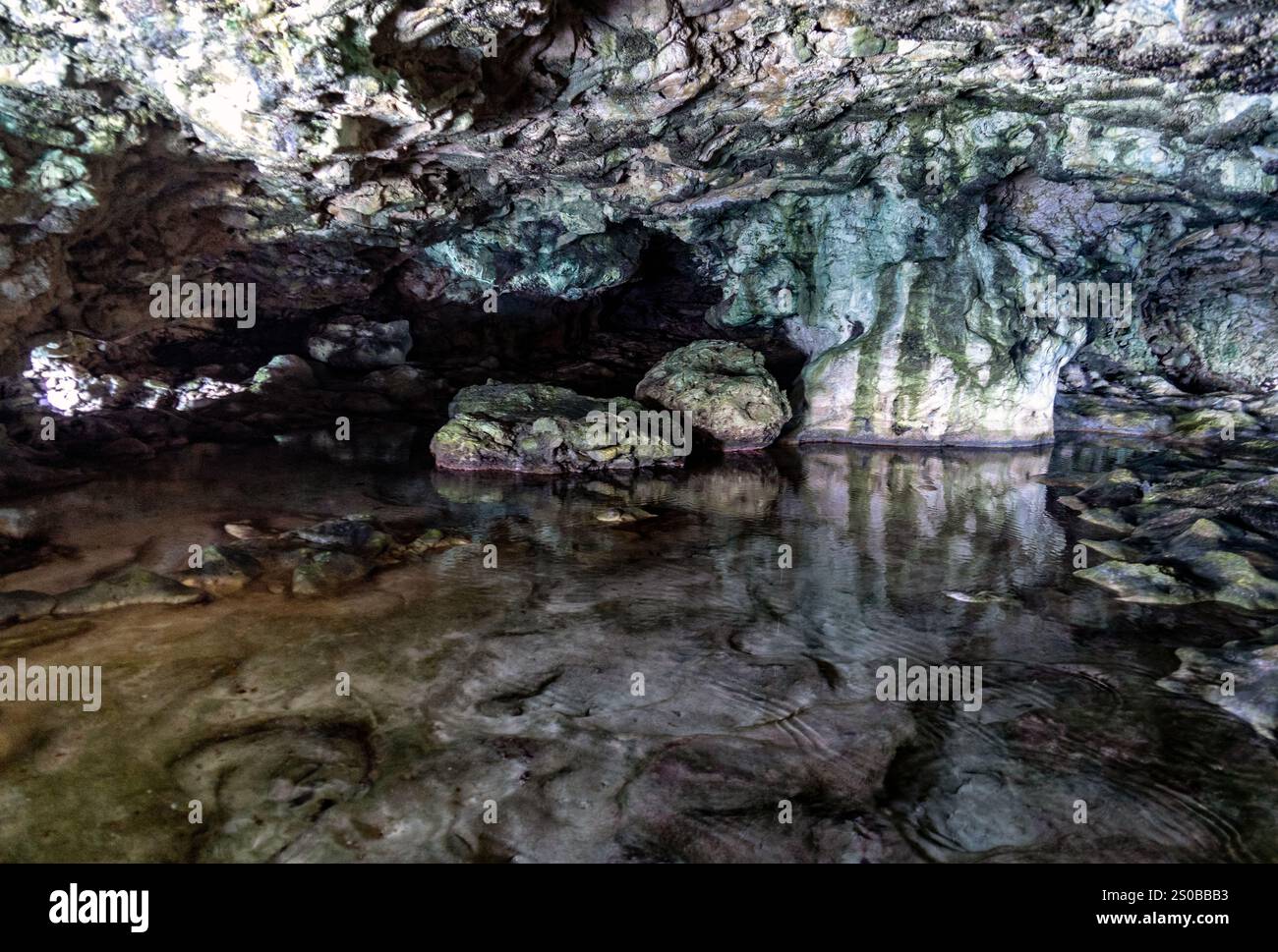 A serene underground cave with rocky formations and a calm water ...