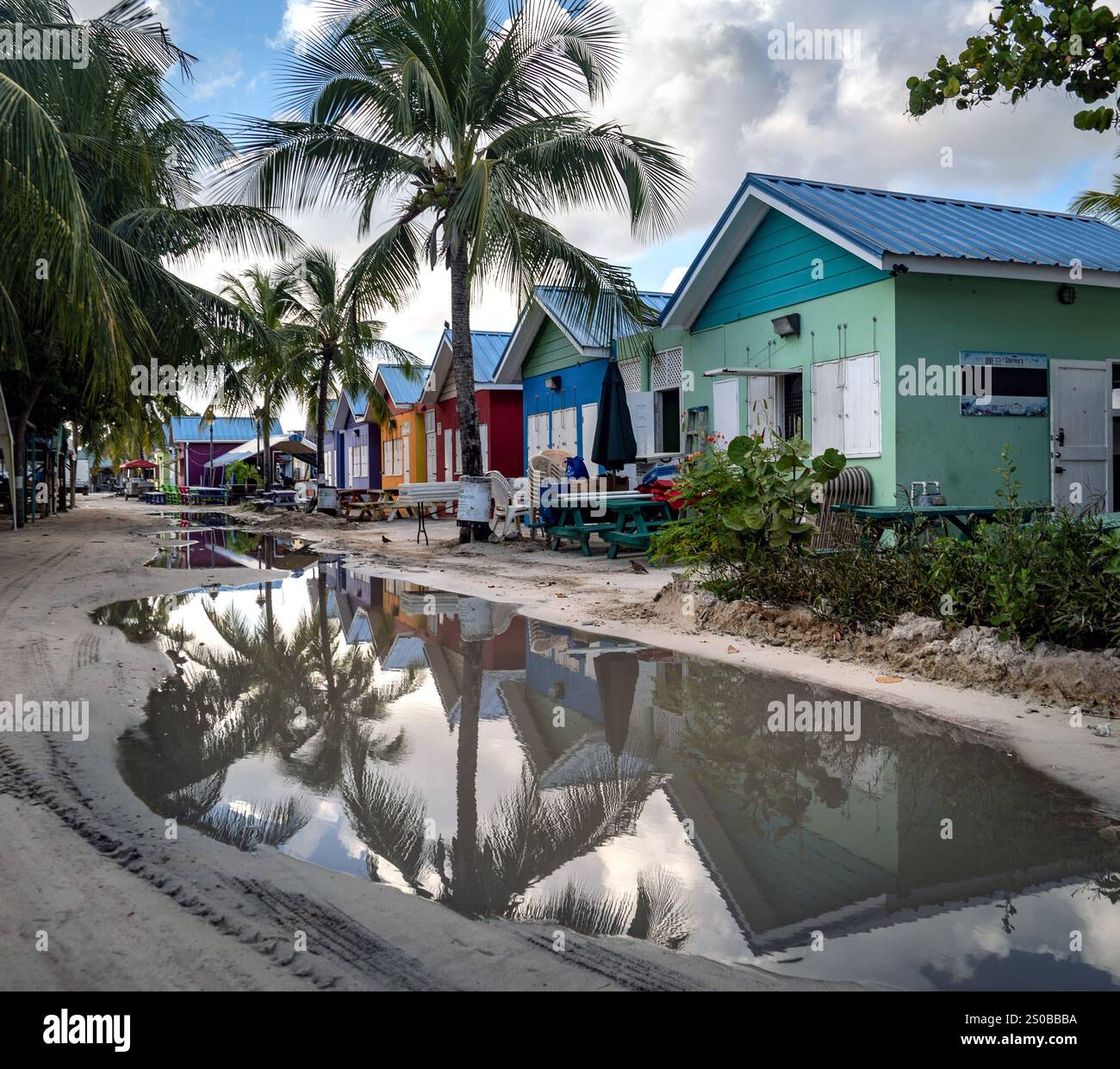 A colorful row of beach houses reflected in a puddle on a sandy street ...