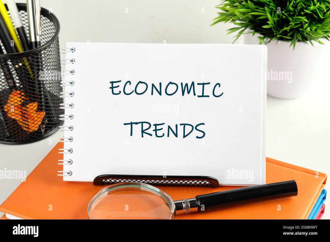 On a desk, a notebook displays the phrase economic trends. A magnifying ...