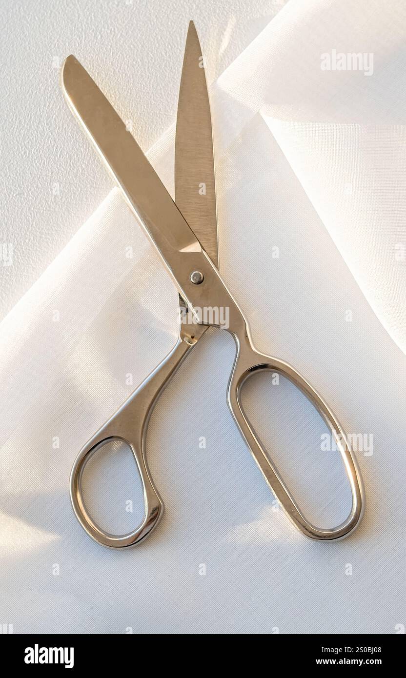 Tailor's steel scissors lying on white transparent fabric, creating ...