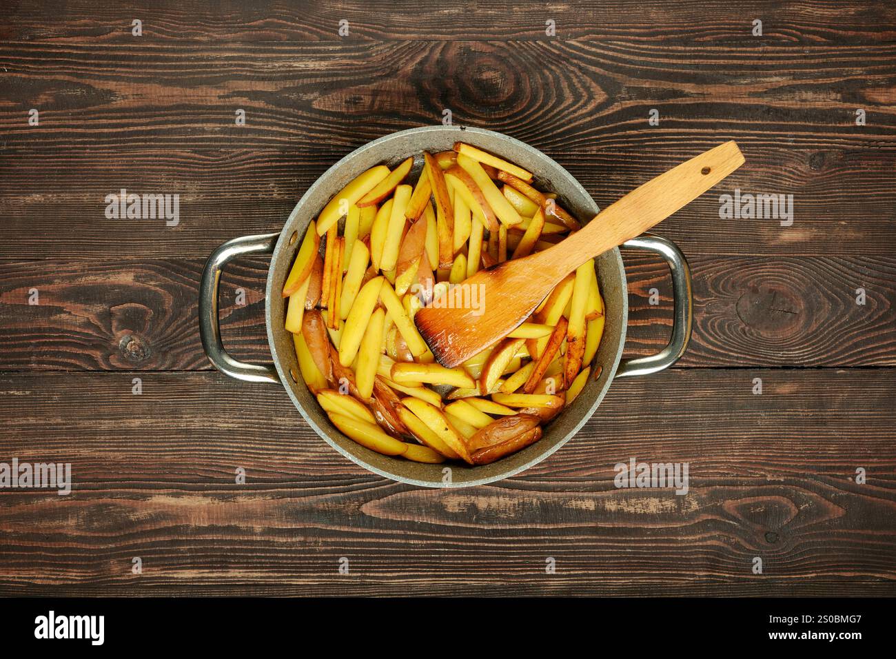 Freshly cut potato fries are frying in a large pot, their golden color ...