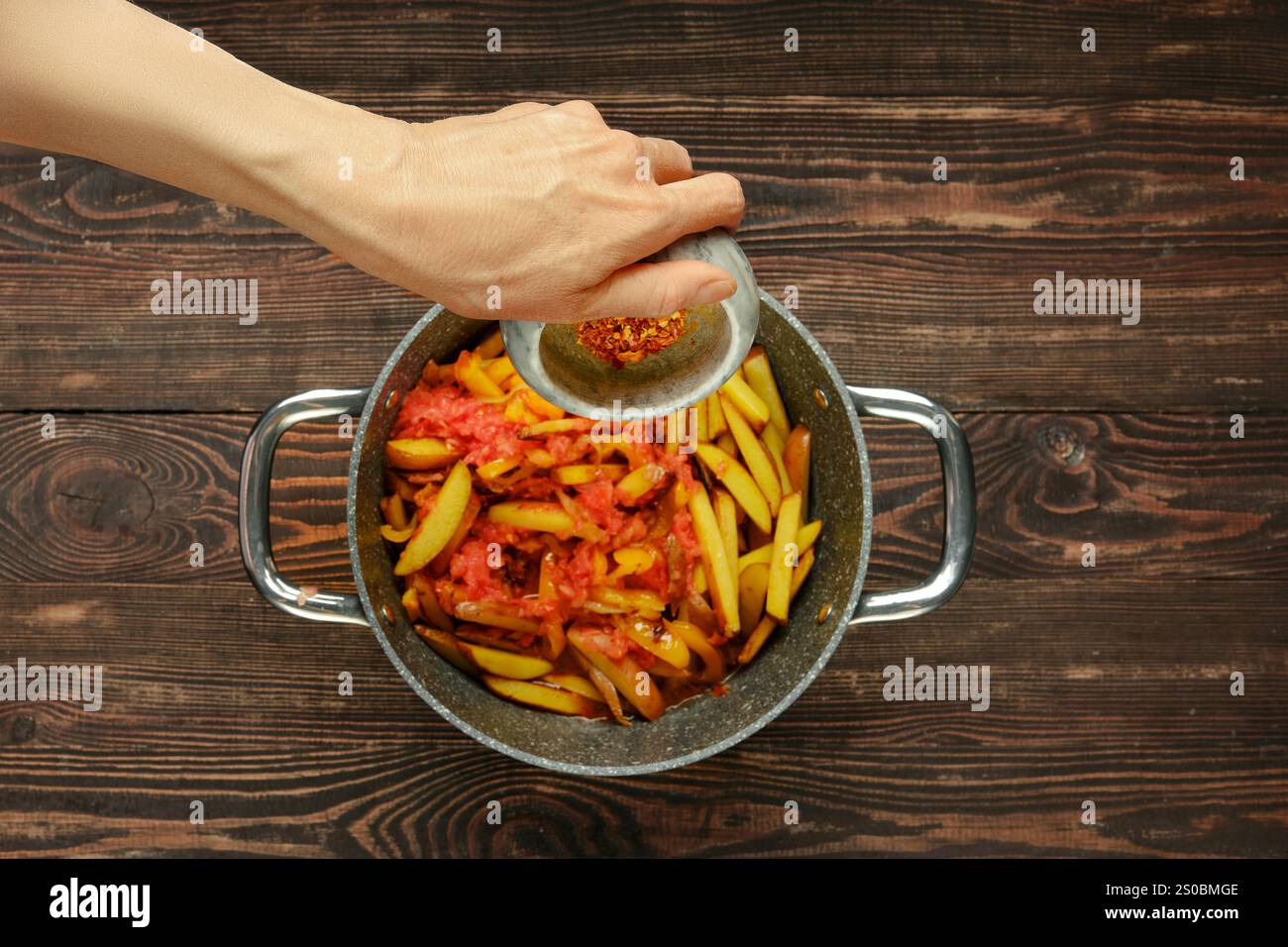 A hand sprinkles chili pepper flakes over a pan filled with fresh ...