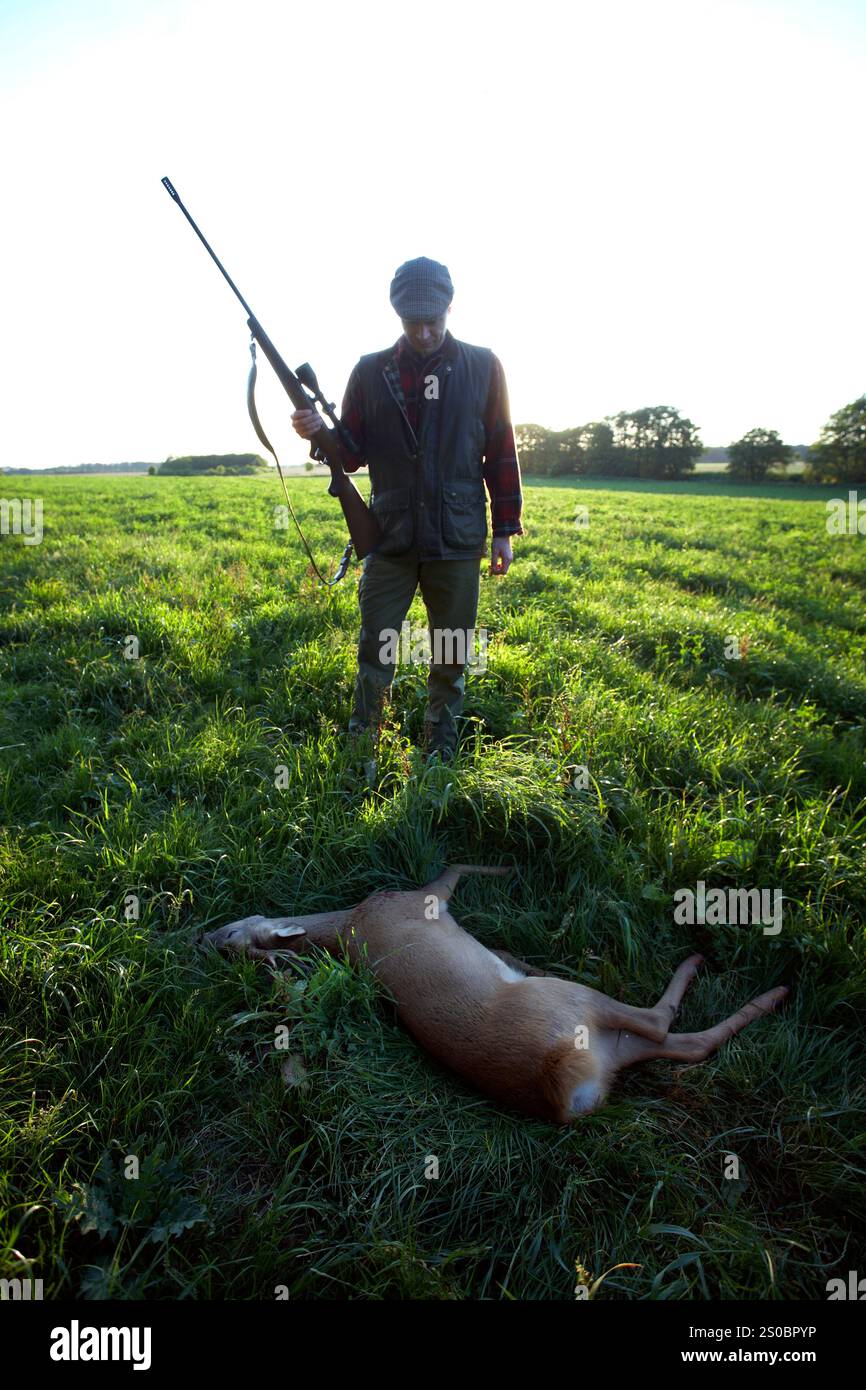 A hunter stands over his kill in a grassy field, during a deer hunting trip in Zealand, Denmark ...