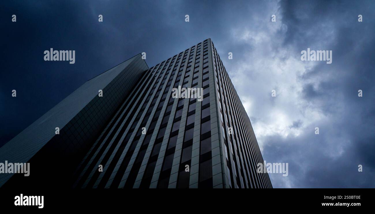A dramatic view of a tall modern building against a moody sky filled ...