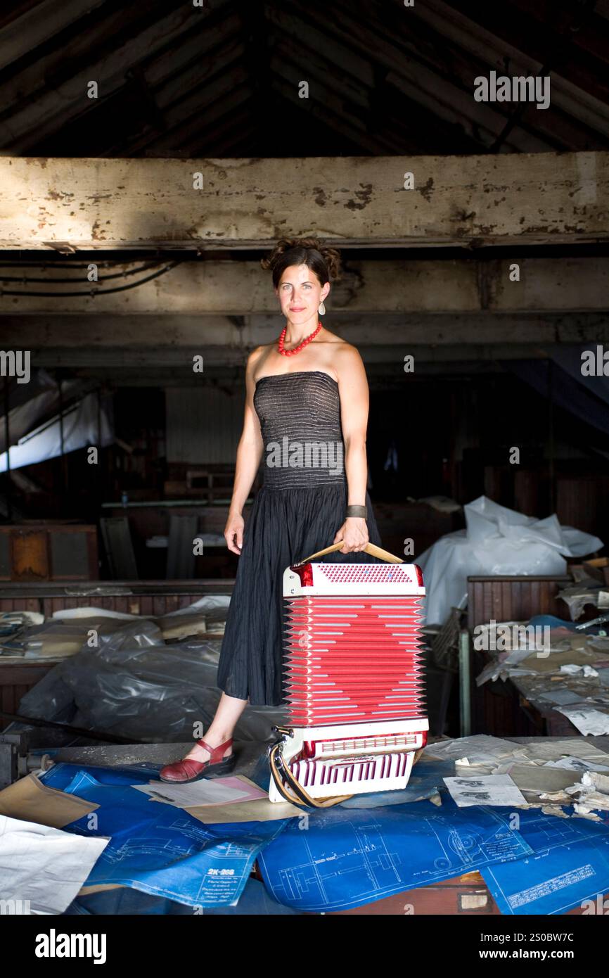 Young woman in black dress standing holding an accordion in cluttered ...
