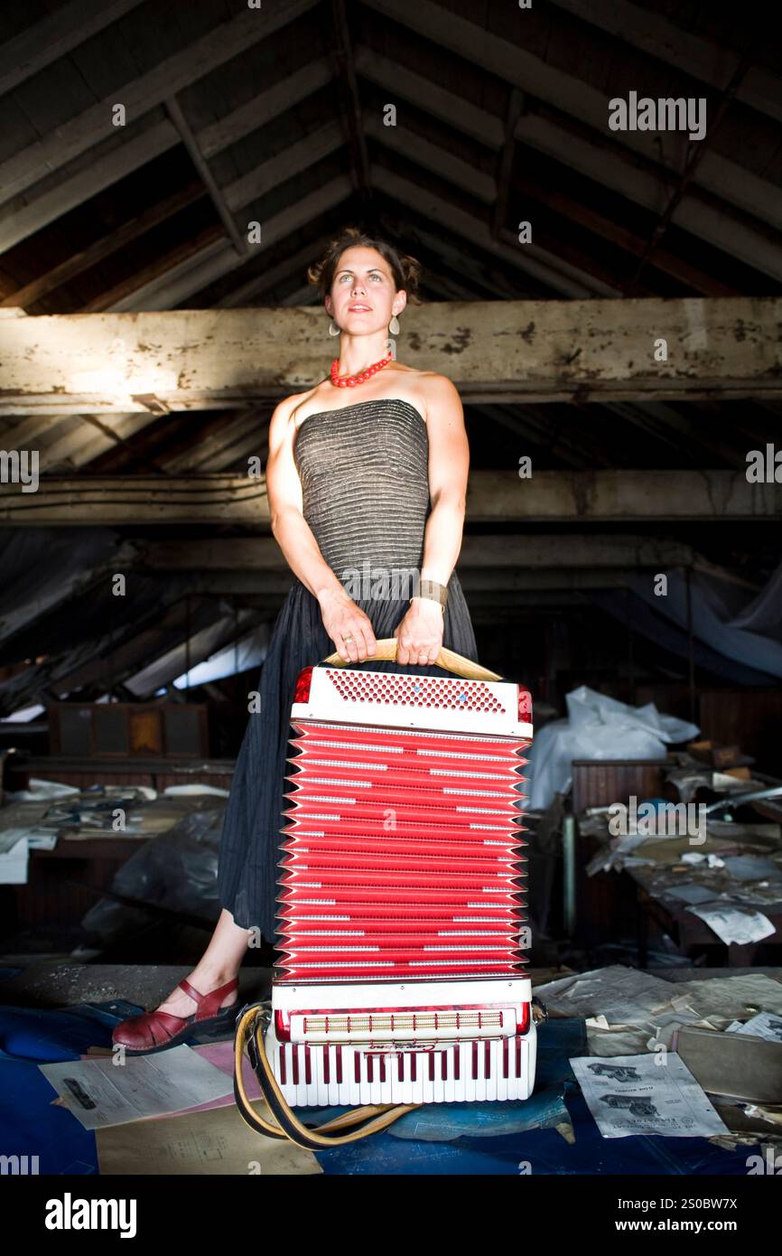 Young woman in black dress standing holding an accordion in cluttered ...