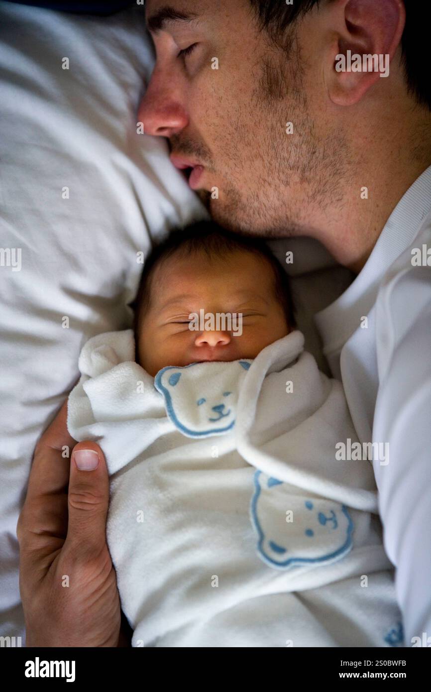 A father naps with his newborn baby daughter who is swaddled in a wrap ...