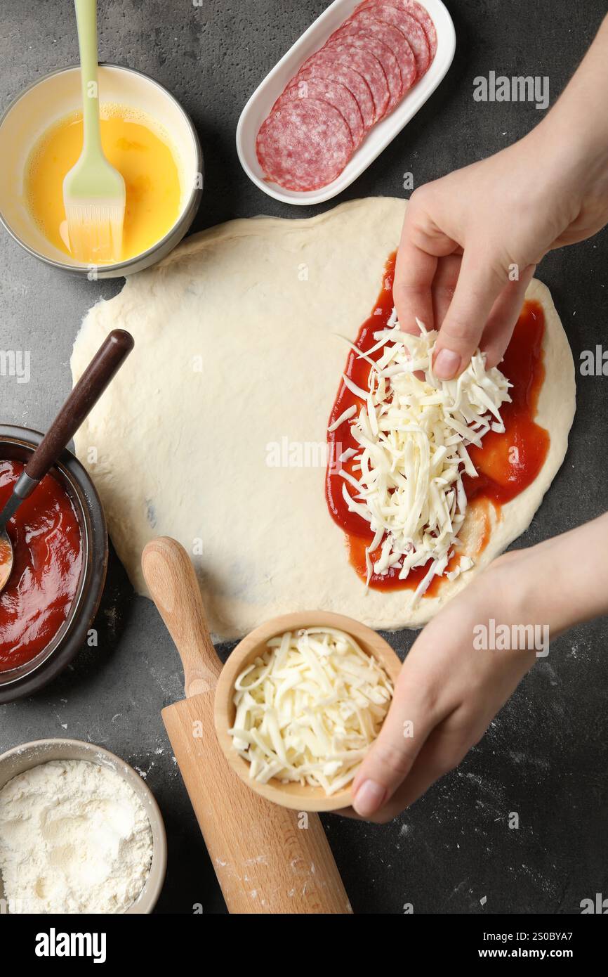 Making calzone pizza. Woman adding cheese on dough at grey table, top ...