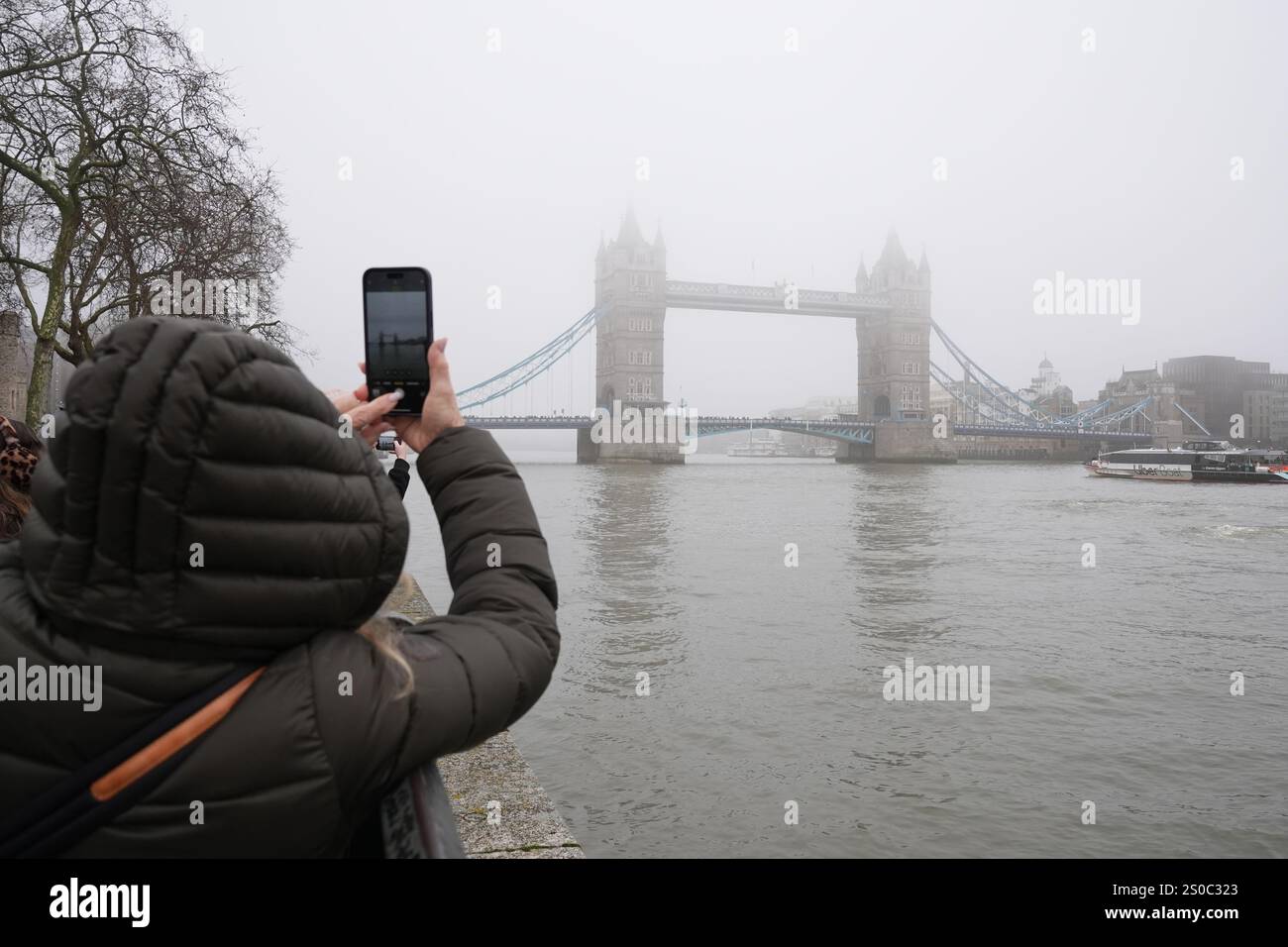 A person takes a photo of Tower Bridge during foggy weather in London ...