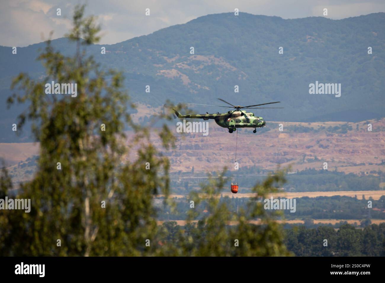 A military helicopter carries water with a helicopter bucket ...