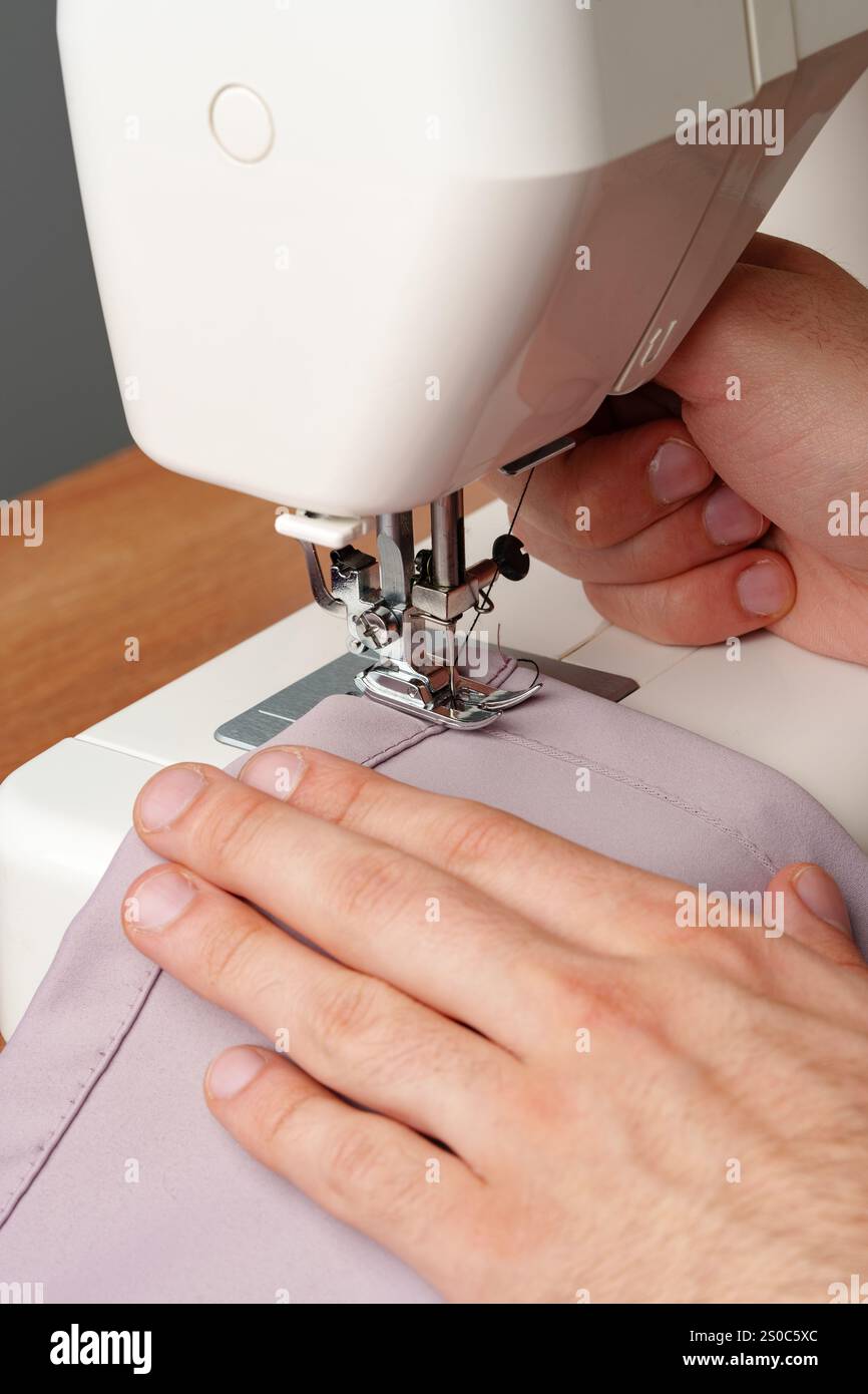 Hands sewing fabric using a sewing machine on a wooden table in a well ...