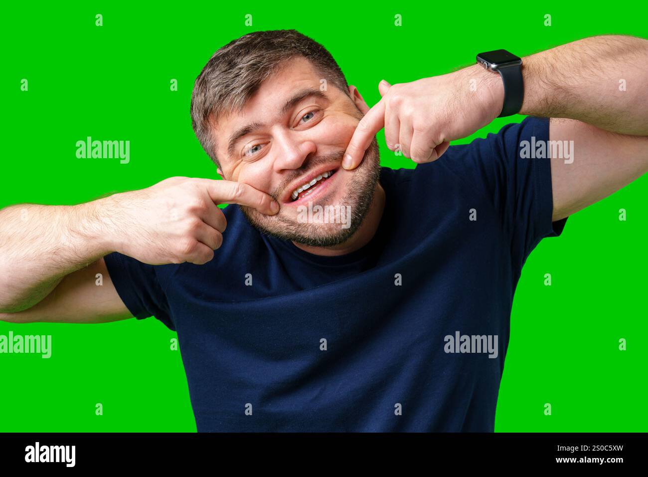 A smiling man playfully poking his cheeks against a vibrant green ...