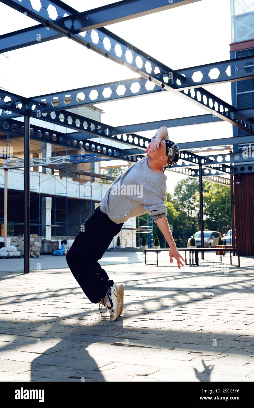 A dancer performs a move under a metal structure in the afternoon sun ...