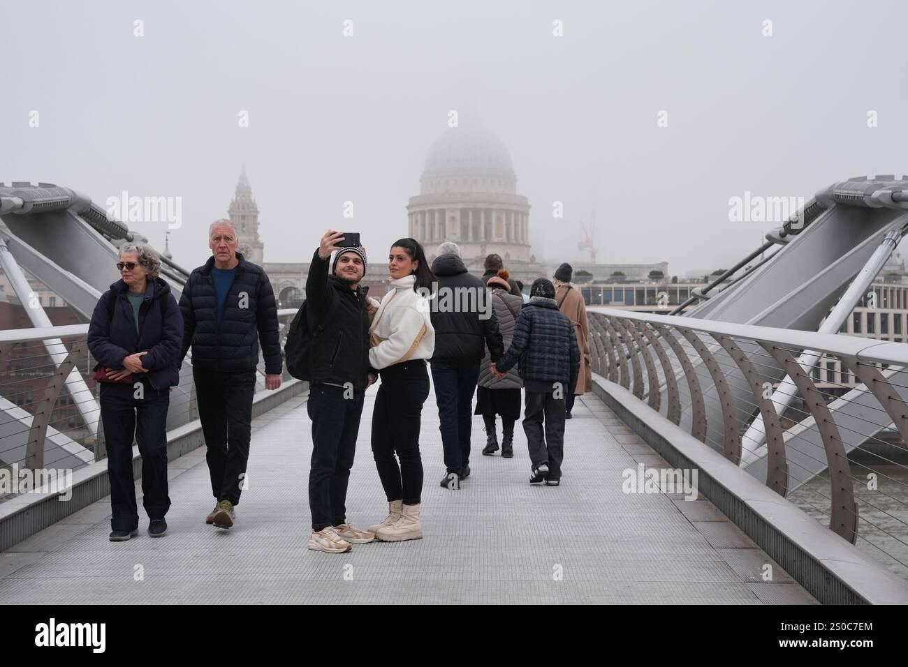 People walk across Millennium Bridge, London, during foggy weather. The ...