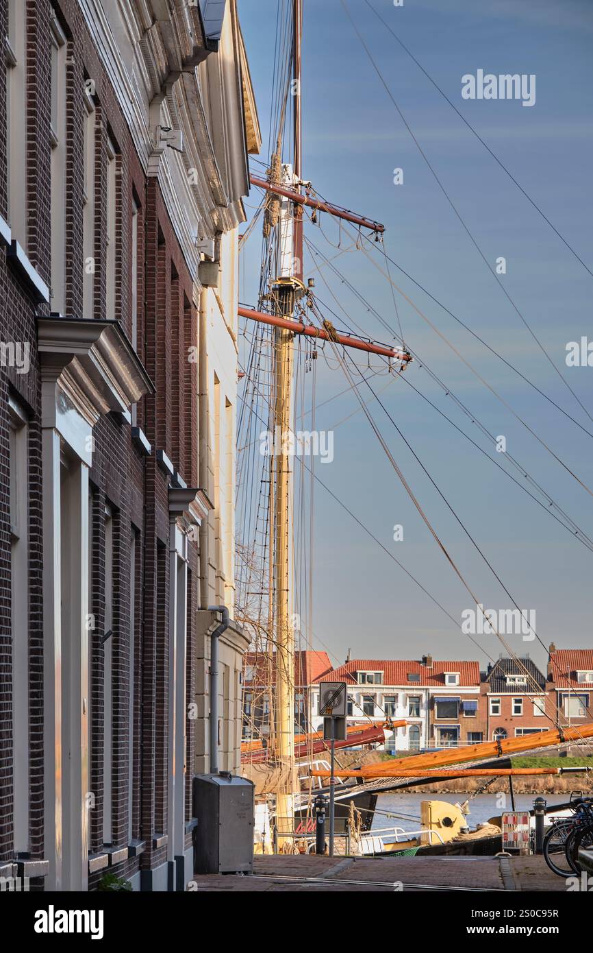 The tall mast of a historic ship rises near Kampen riverside, framed by ...