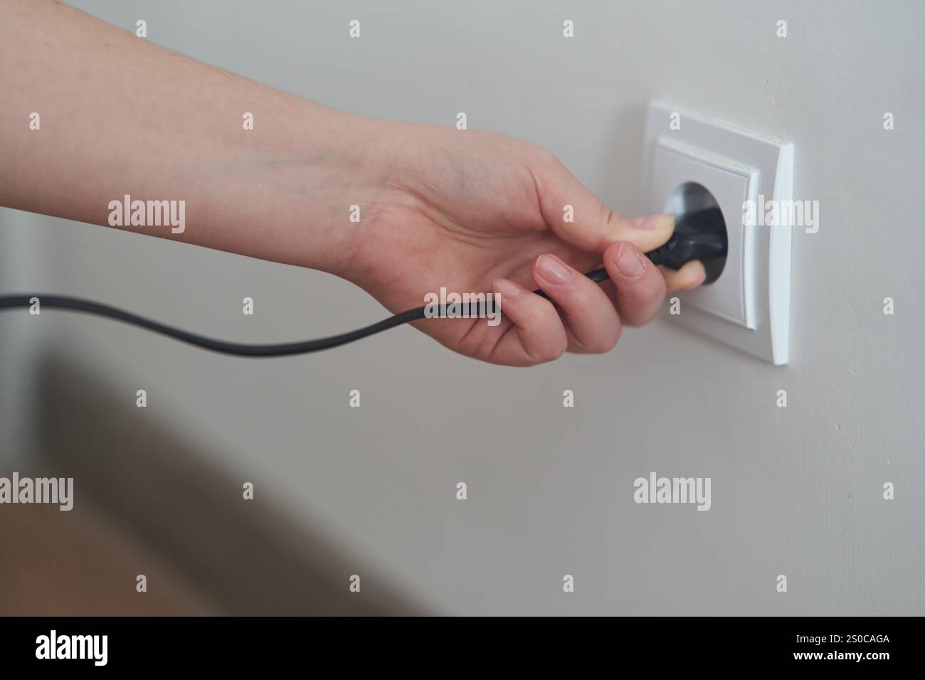 A young girl inserts a plug into an outlet. Young woman plugs the phone ...