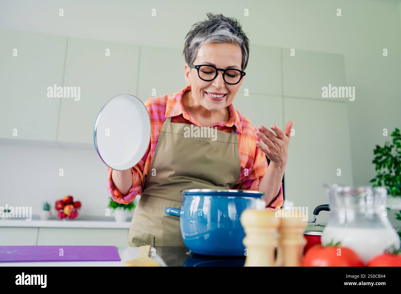 Beautiful elderly woman joyfully cooking in the kitchen, wearing an ...