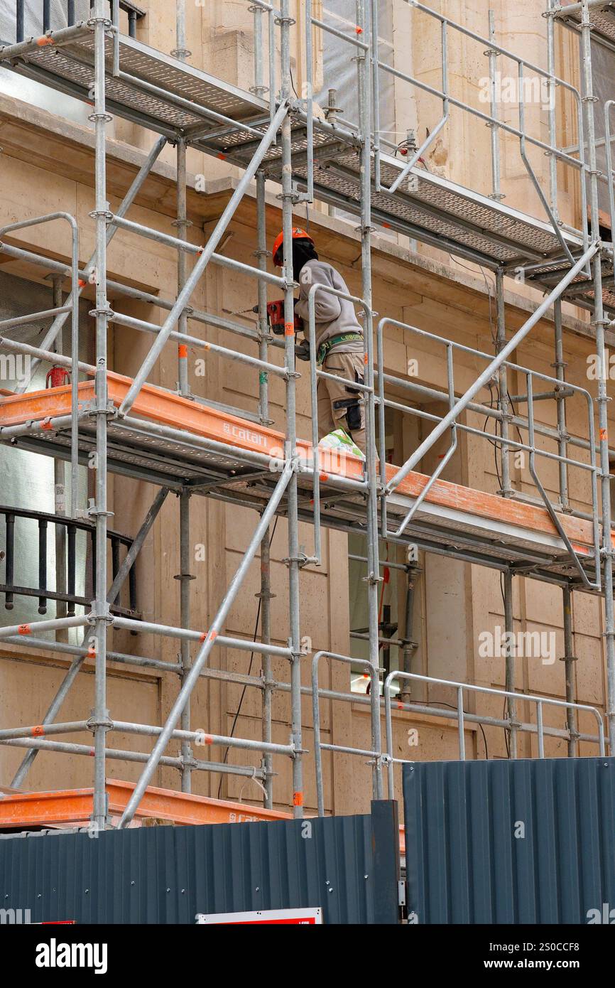 Construction worker using power tools to work on building facade while ...
