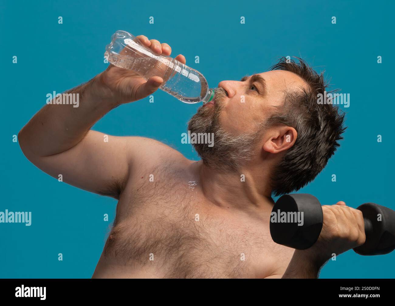 An elderly man lifts a dumbbell while drinking water to stay hydrated ...