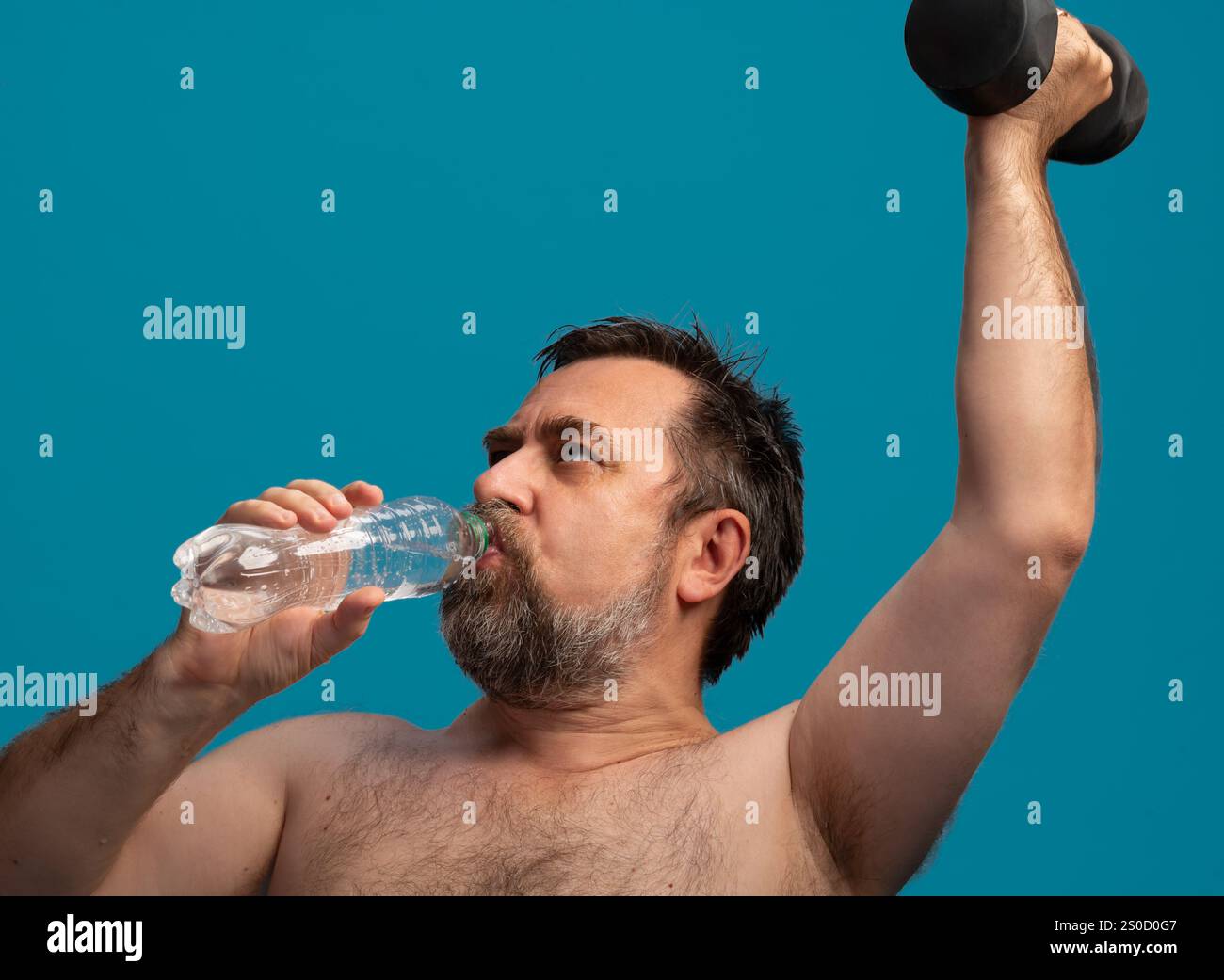 An elderly man lifts a dumbbell while drinking water to stay hydrated ...