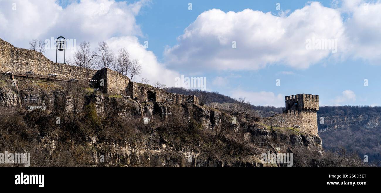 A medieval stone fortress on a rocky hilltop under a blue sky with ...