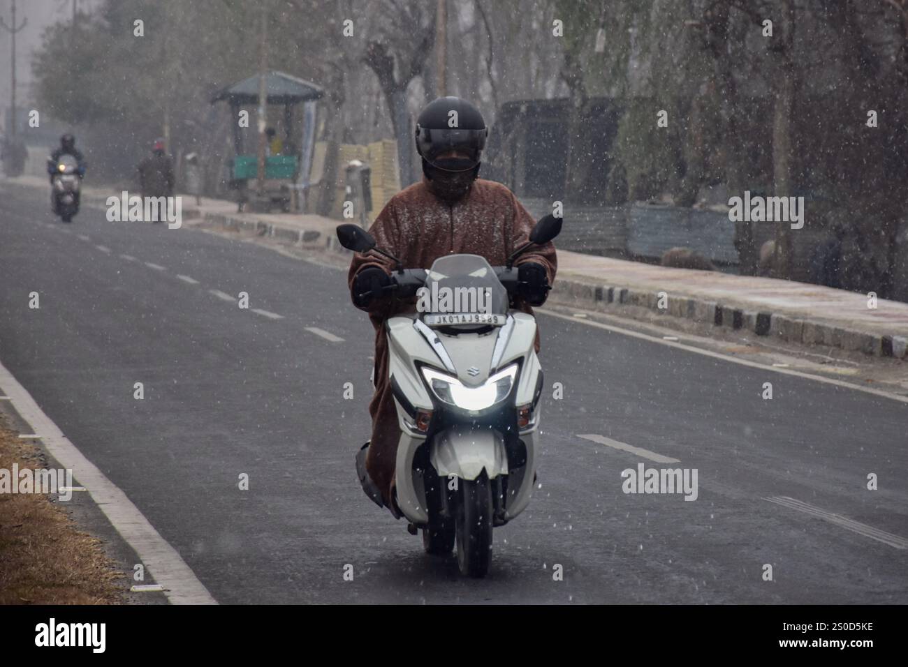 A man rides a scooter along the snow covered road during seasons first snowfall in Srinagar, the ...